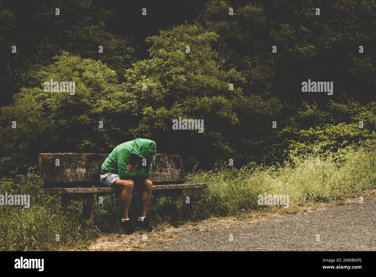 Hooded man sitting on a bench in a park looking depressed. Personality ...