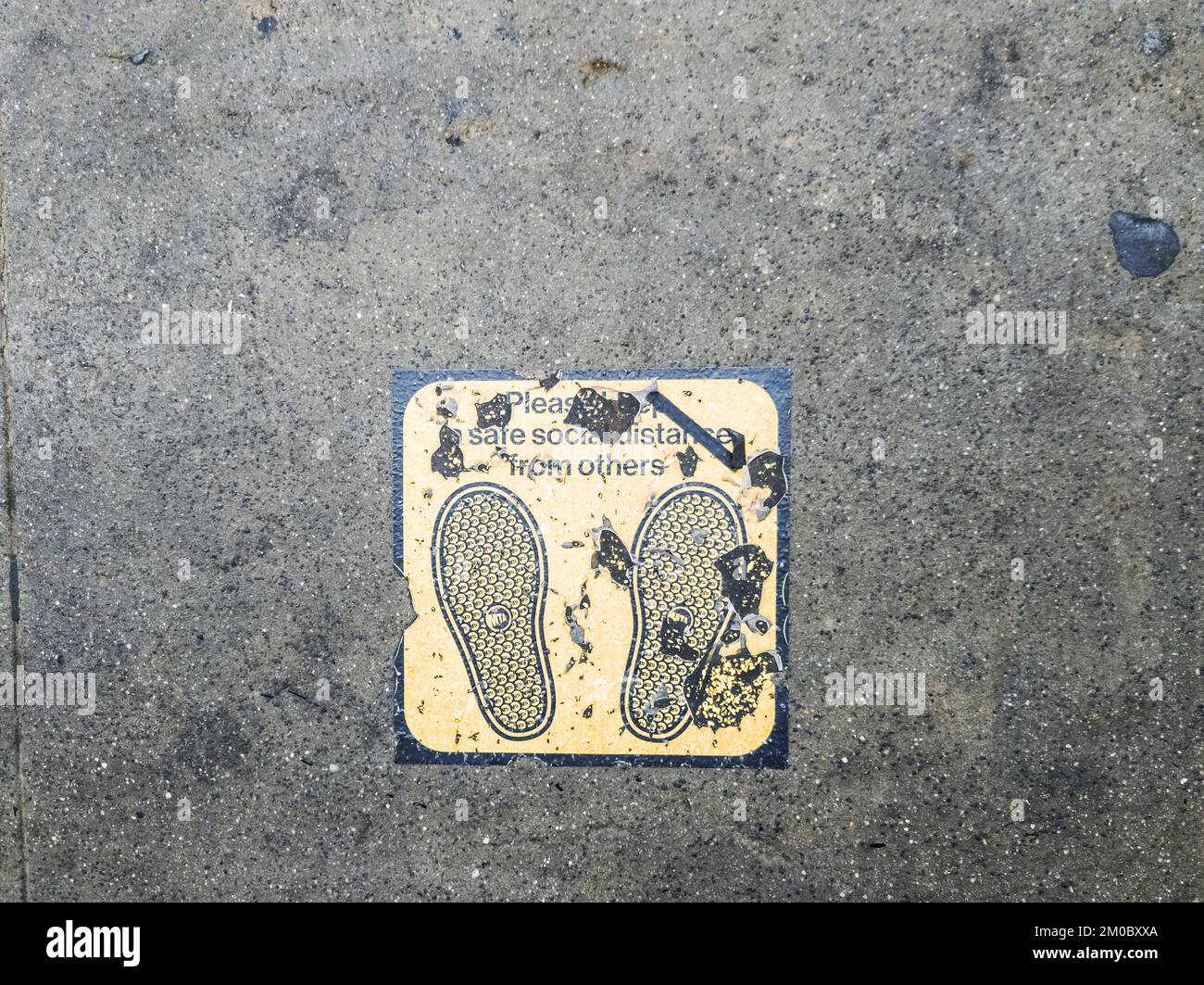 A worn social distancing sticker on the floor of a platform in a subway ...