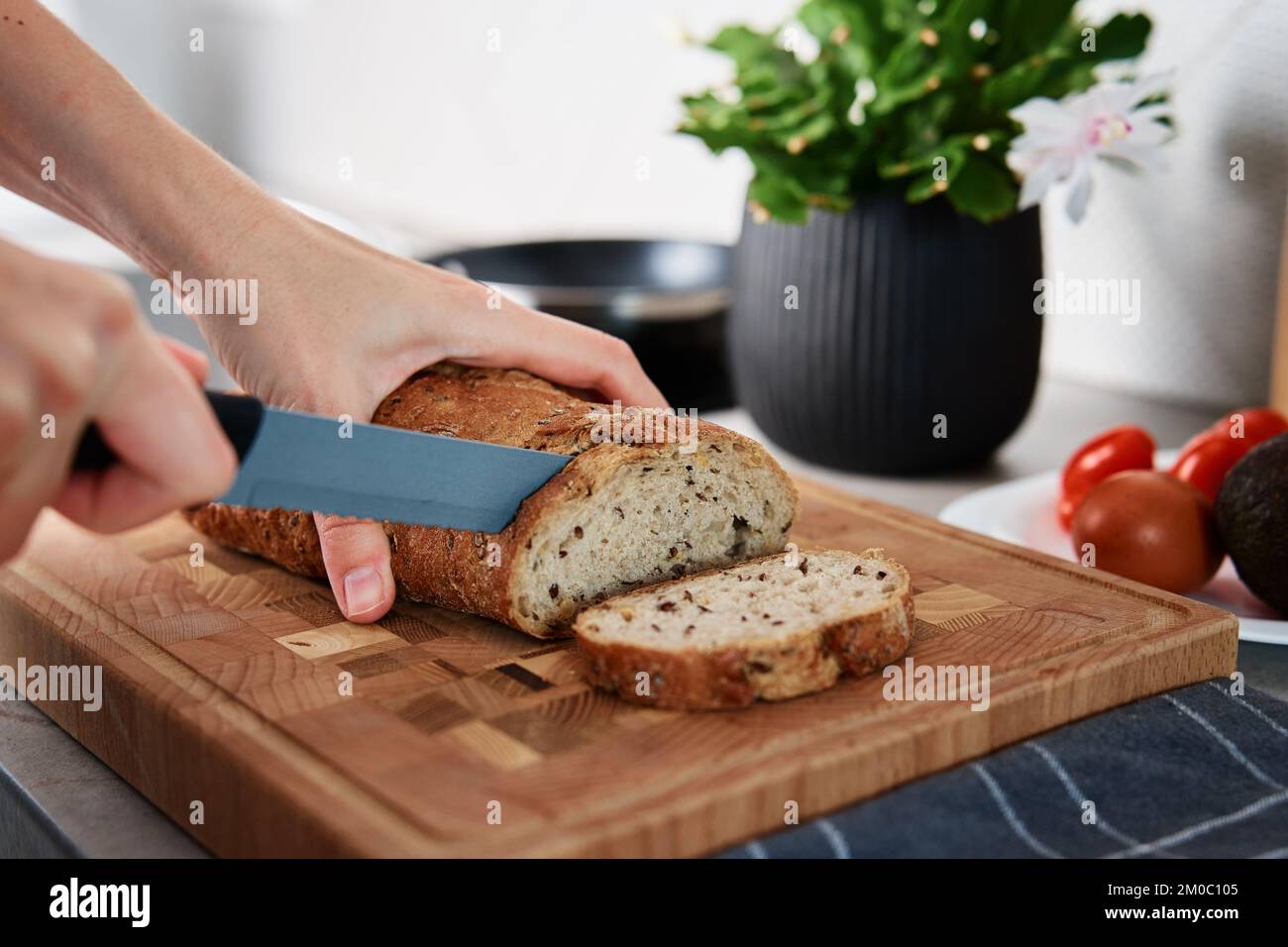 Woman cutting loaf of whole grain bread with large knife on cutting ...