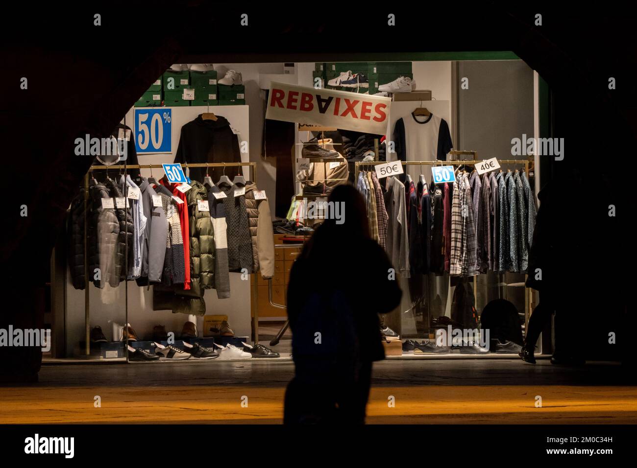 Woman looking at illuminated window of clothing store with sale and ...