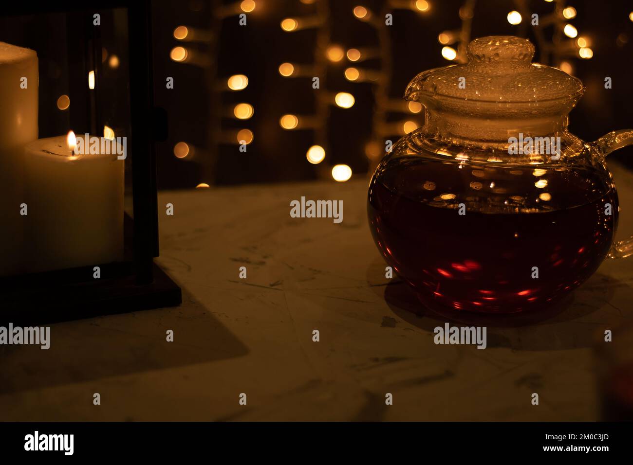 photo glass teapot with tea next to a candle and glowing lights in the ...
