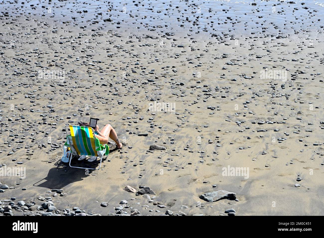 Person sunbathing on sandy beach with pebbles sitting on folding chair ...