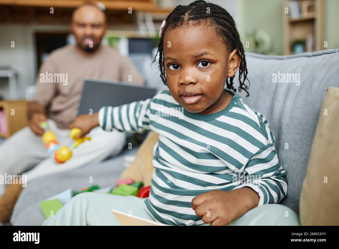 Portrait of cute black child looking at camera while playing on couch ...