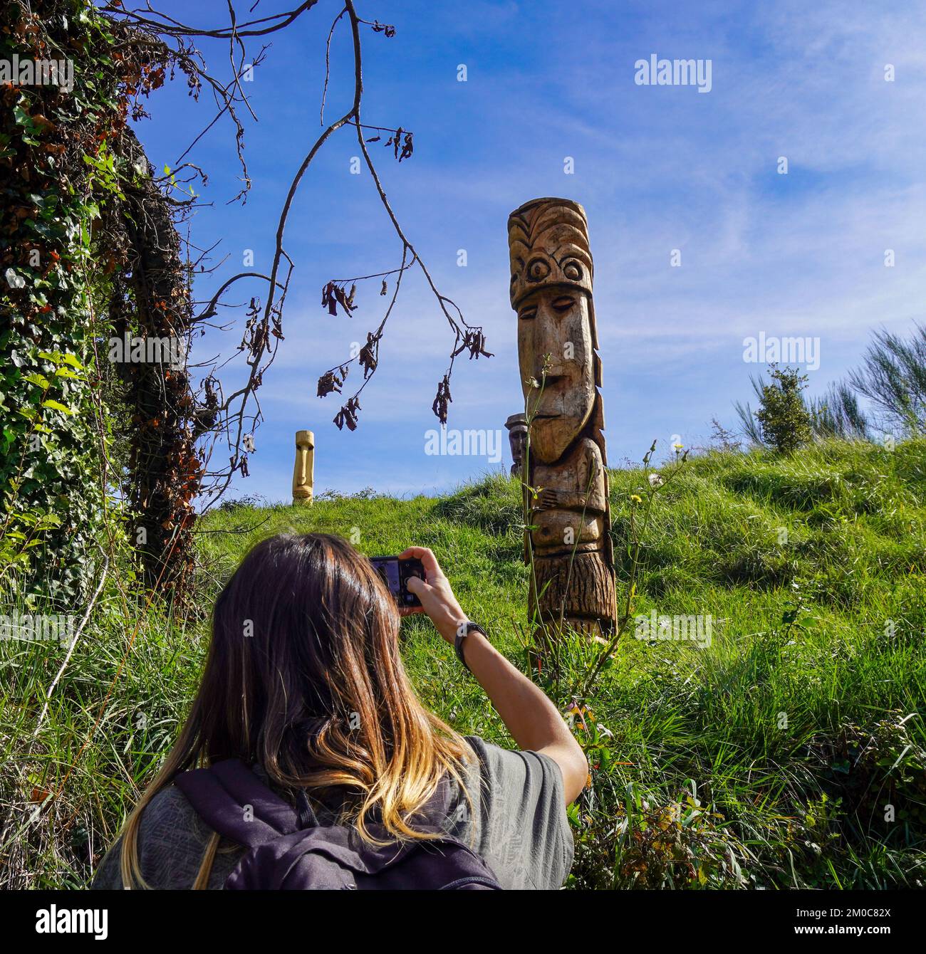 Long-haired young woman taking a picture of a wooden moai crouched in ...