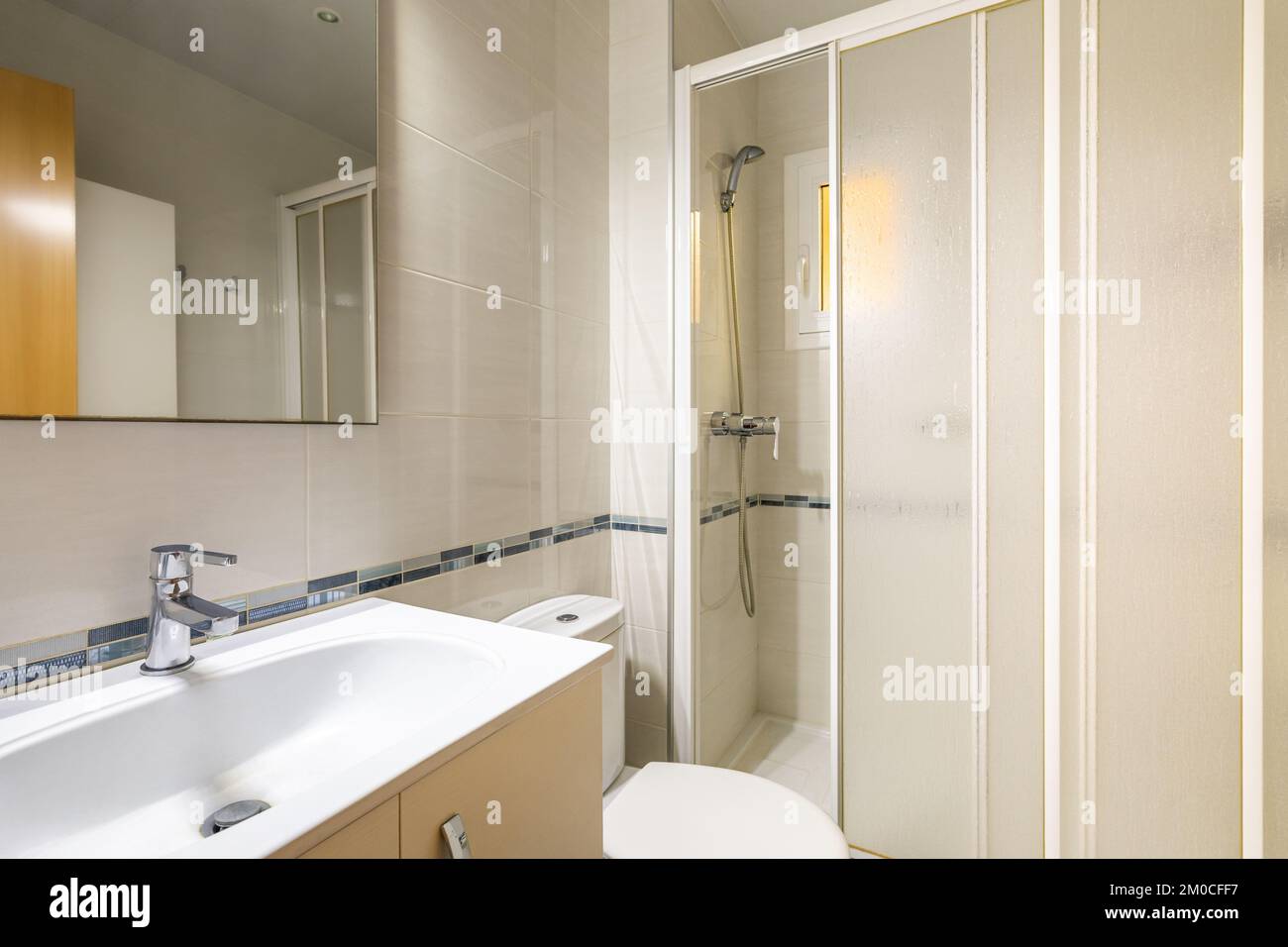 Interior of modern tiled bathroom with white sink, wooden furniture ...