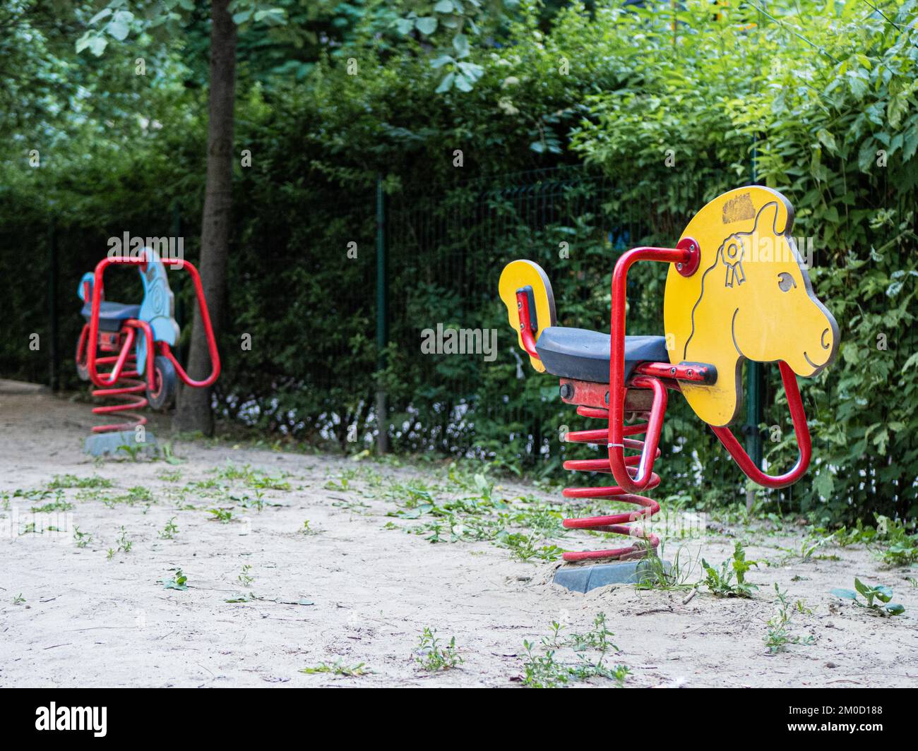 Yellow horse and blue motorbike spring swing toys at a sandy green ...