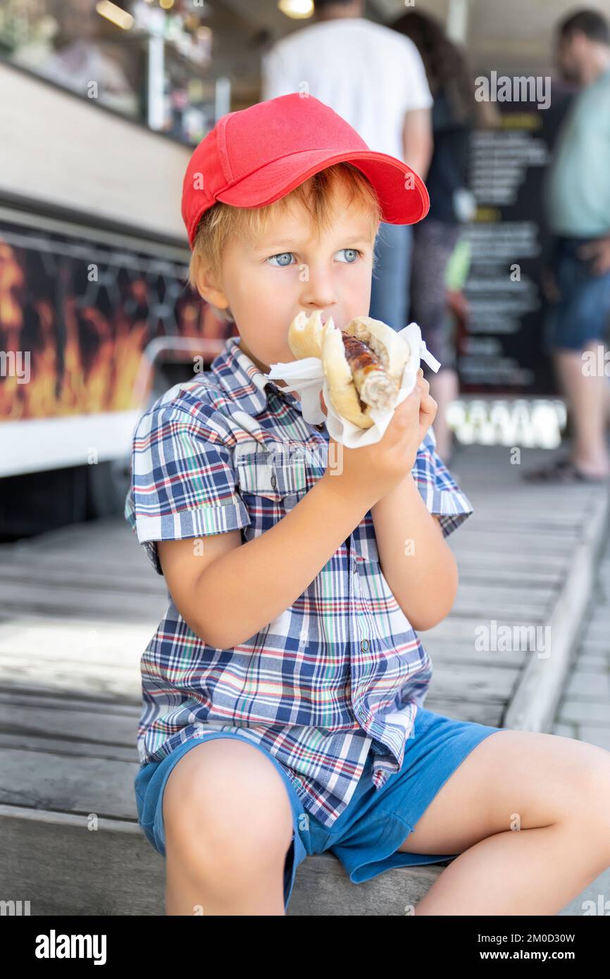 Cute adorable pensive little boy kid enjoy eating hot dog sausage in ...
