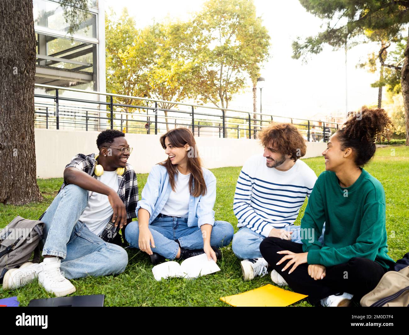 Group of diverse college student friends laughing and chatting sitting on the grass on campus ...