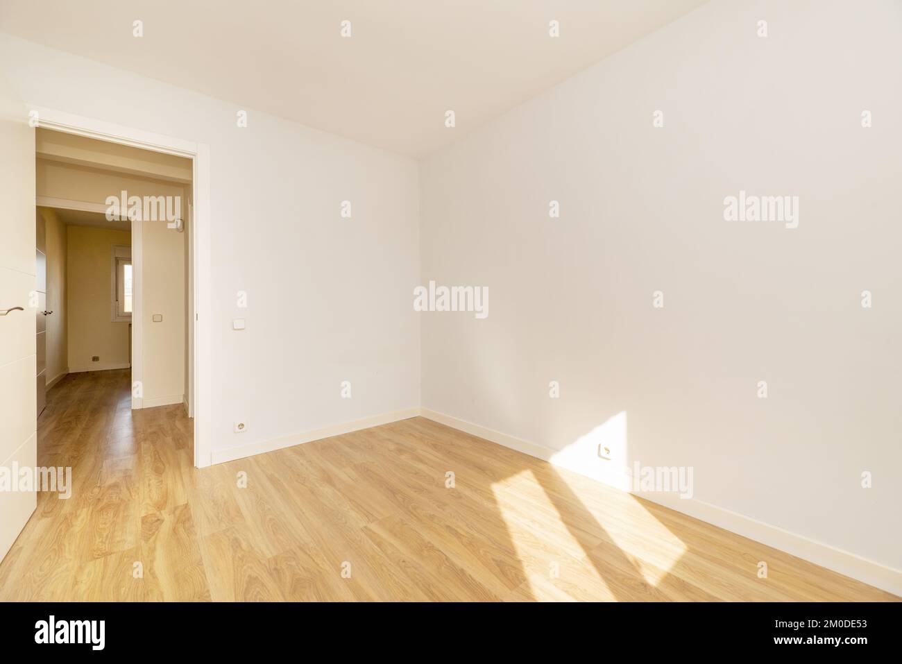 An empty living room with oak type wood laminate flooring and freshly painted plain white walls ...
