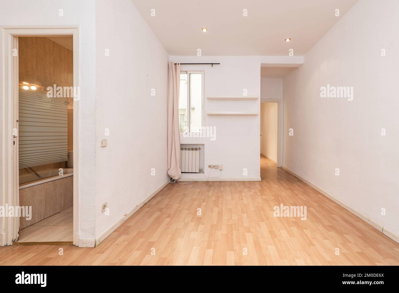 Empty living room with access to a bathroom and a small window with ...