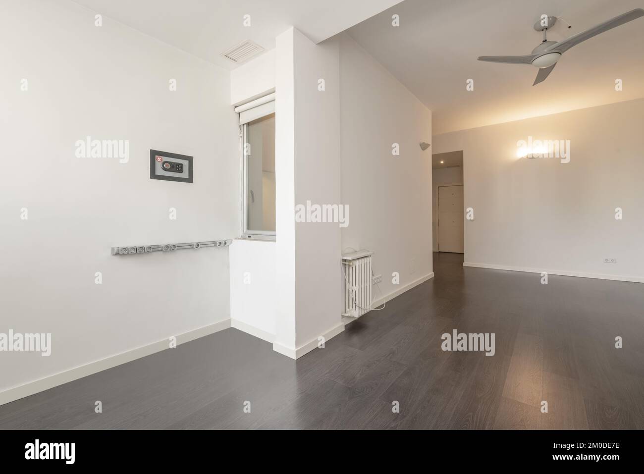 Empty living room of a house with dark laminated flooring, white plain walls and a small built ...