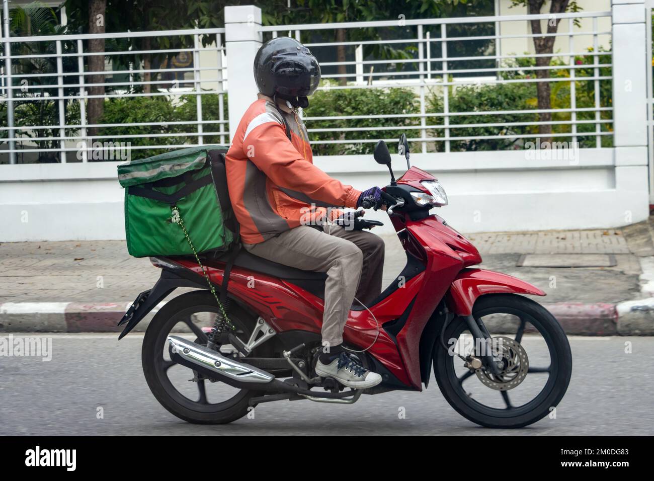 A delivery worker rides a motorcycle with a delivery box, Bangkok ...