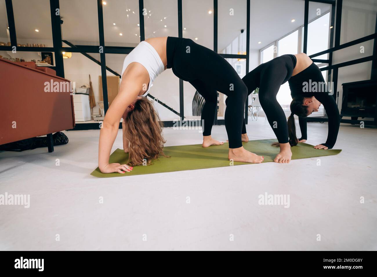 Two young woman practices bridge pose standing on a yoga mat Stock ...