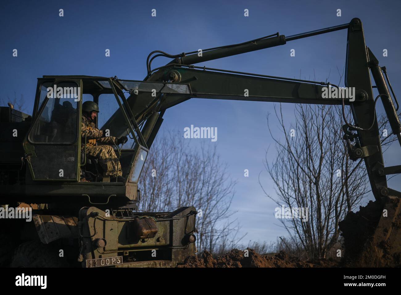 A Ukrainian servicemember digs a trench using an excavator machine in ...