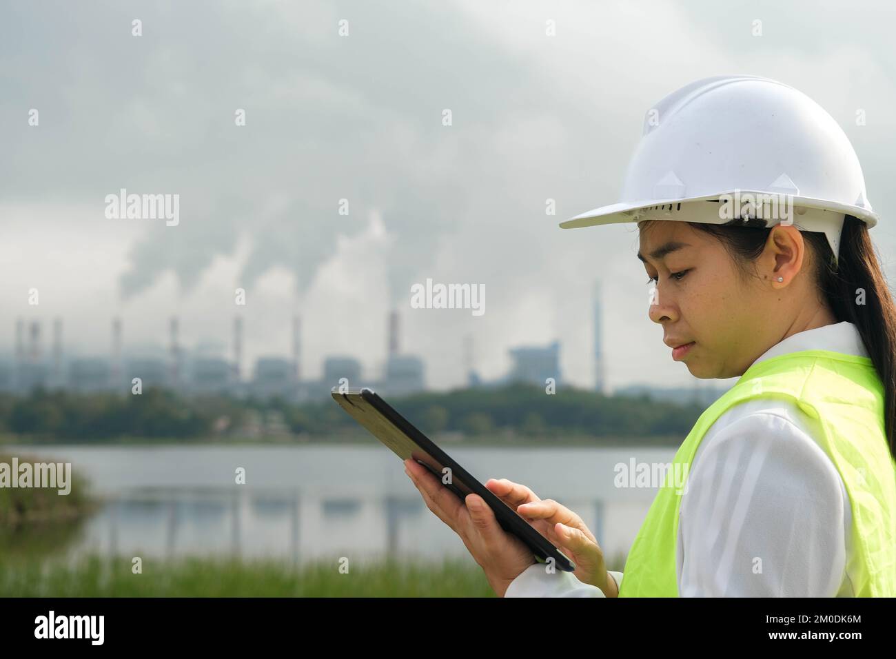 Female chief engineer wearing a green vest and helmet stands outside ...