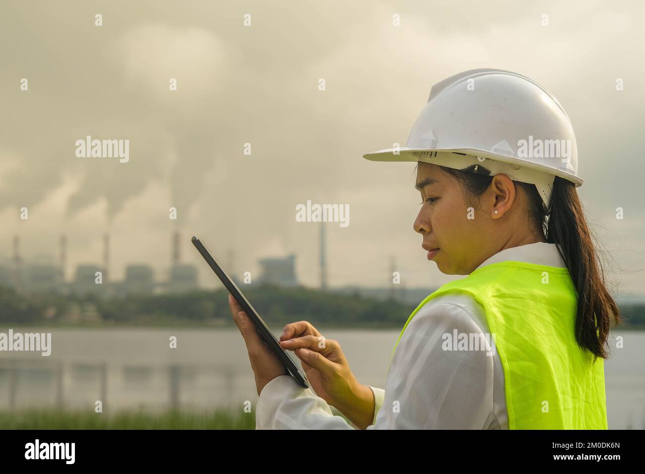 Female chief engineer wearing a green vest and helmet stands outside ...