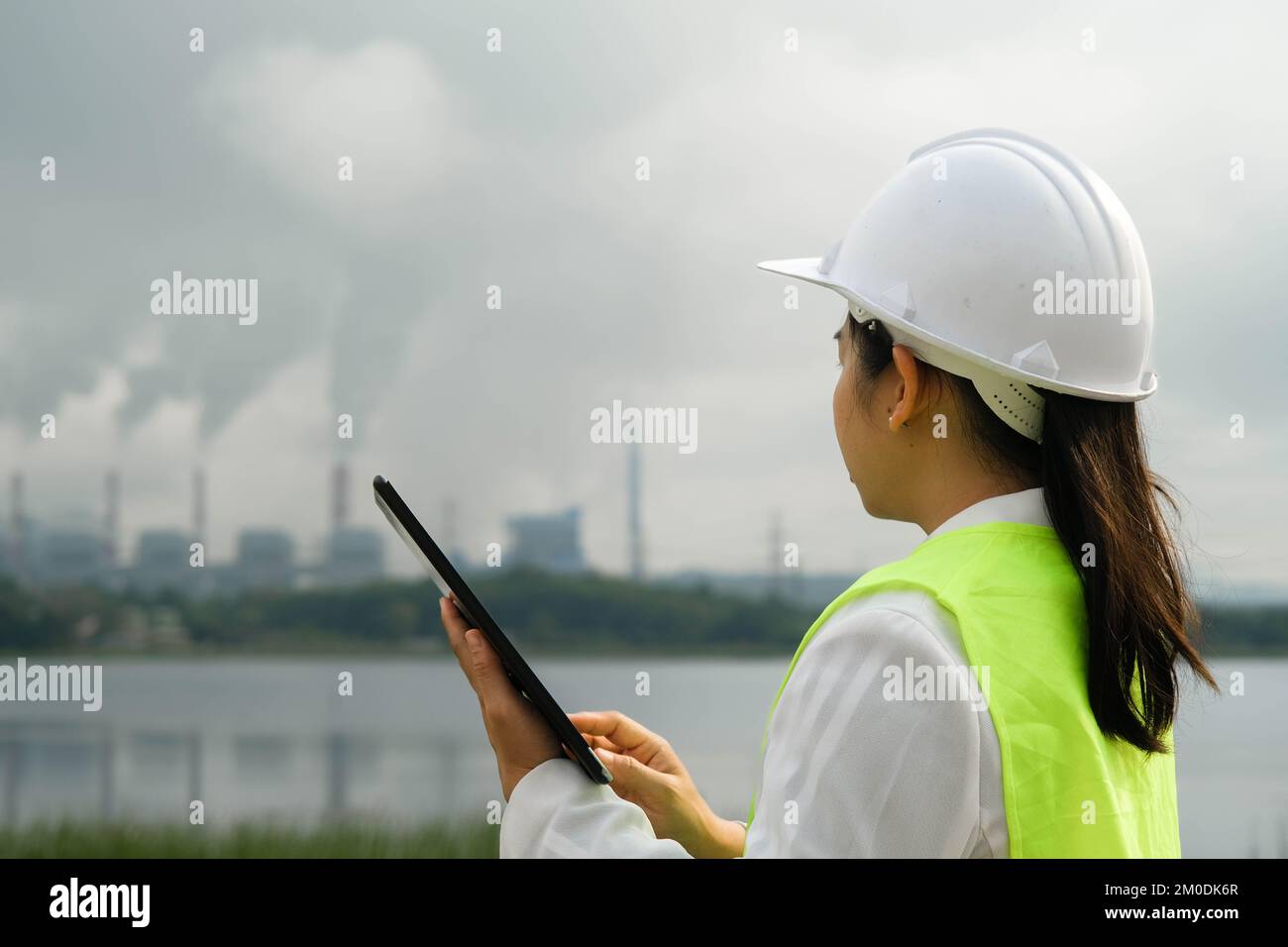 Female chief engineer wearing a green vest and helmet stands outside ...