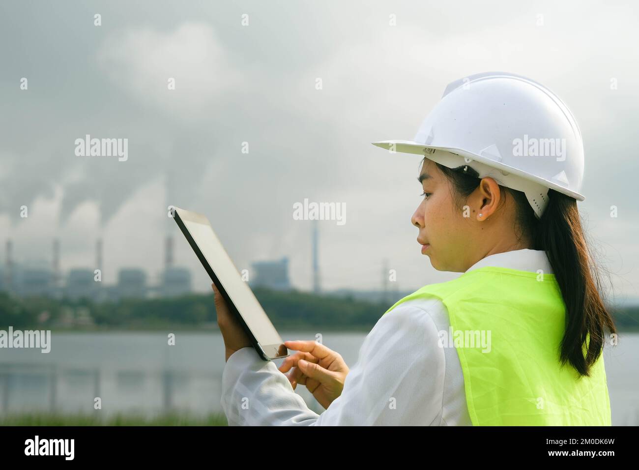 Female chief engineer wearing a green vest and helmet stands outside ...