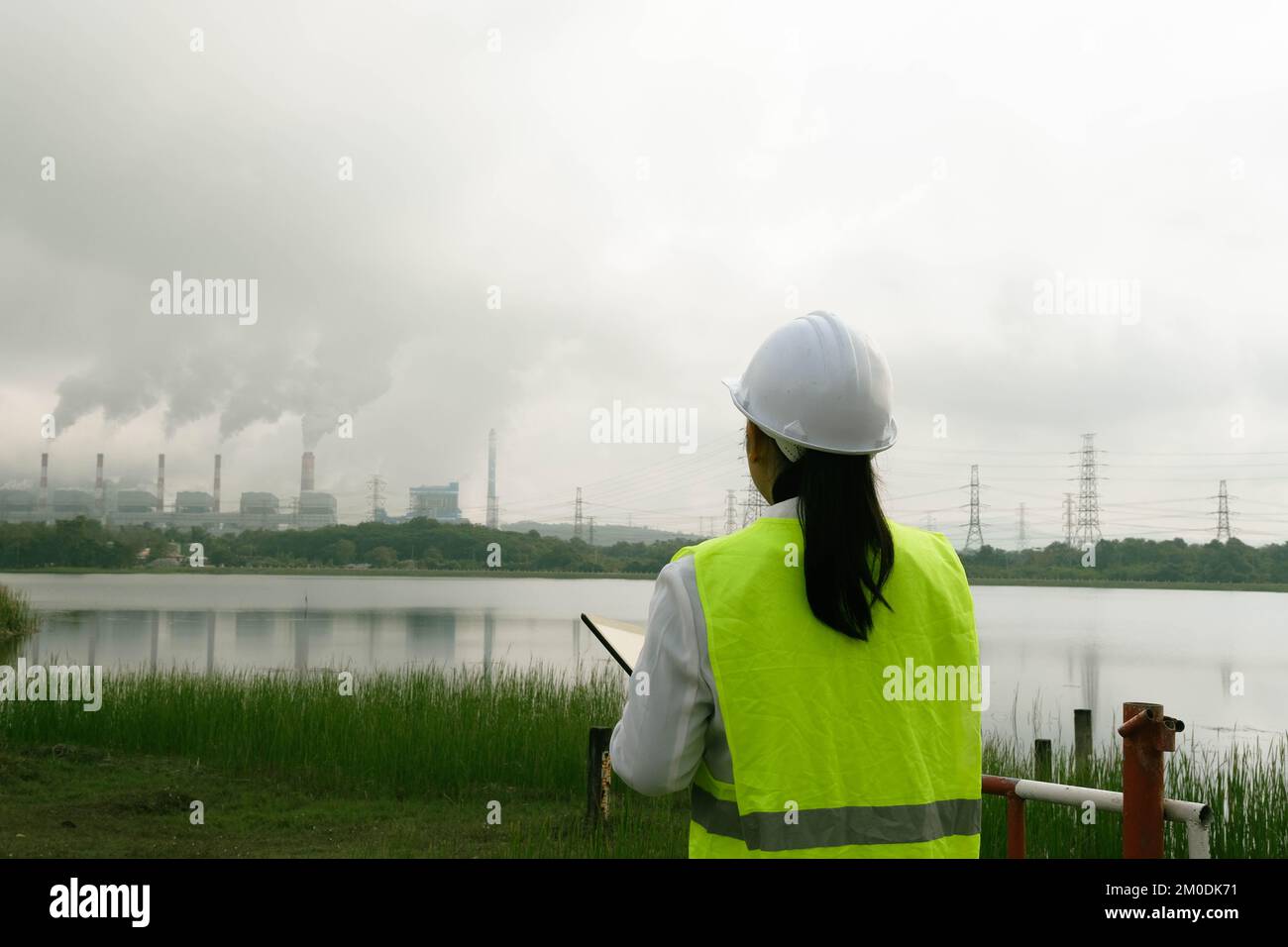 Female chief engineer wearing a green vest and helmet stands outside ...