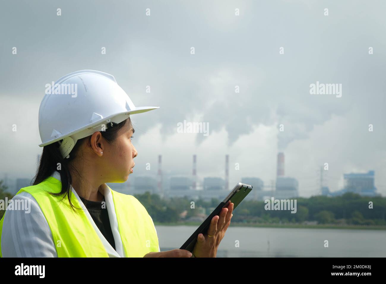 Female chief engineer wearing a green vest and helmet stands outside ...