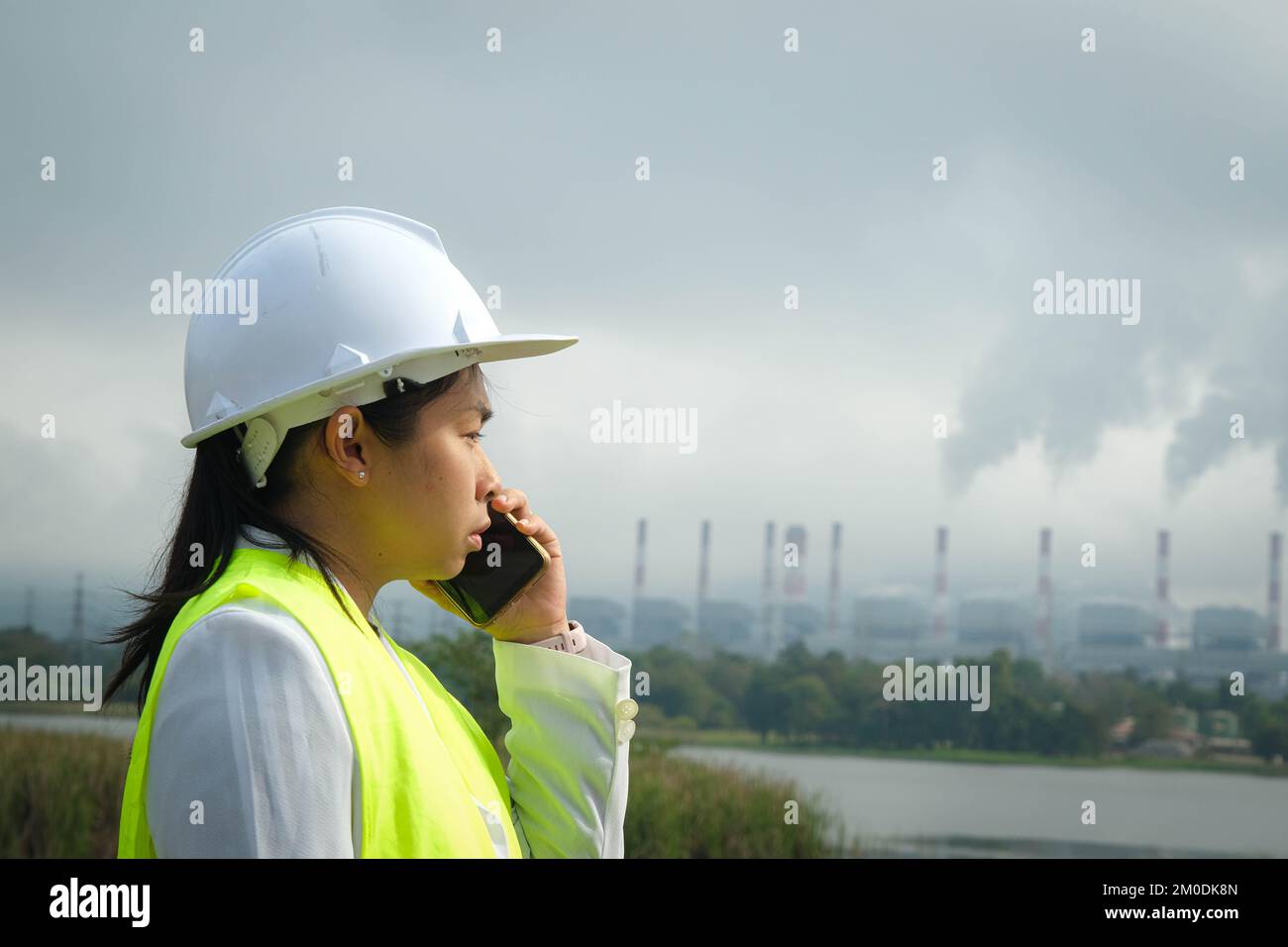 Female chief engineer in green vest and helmet talking on the phone ...