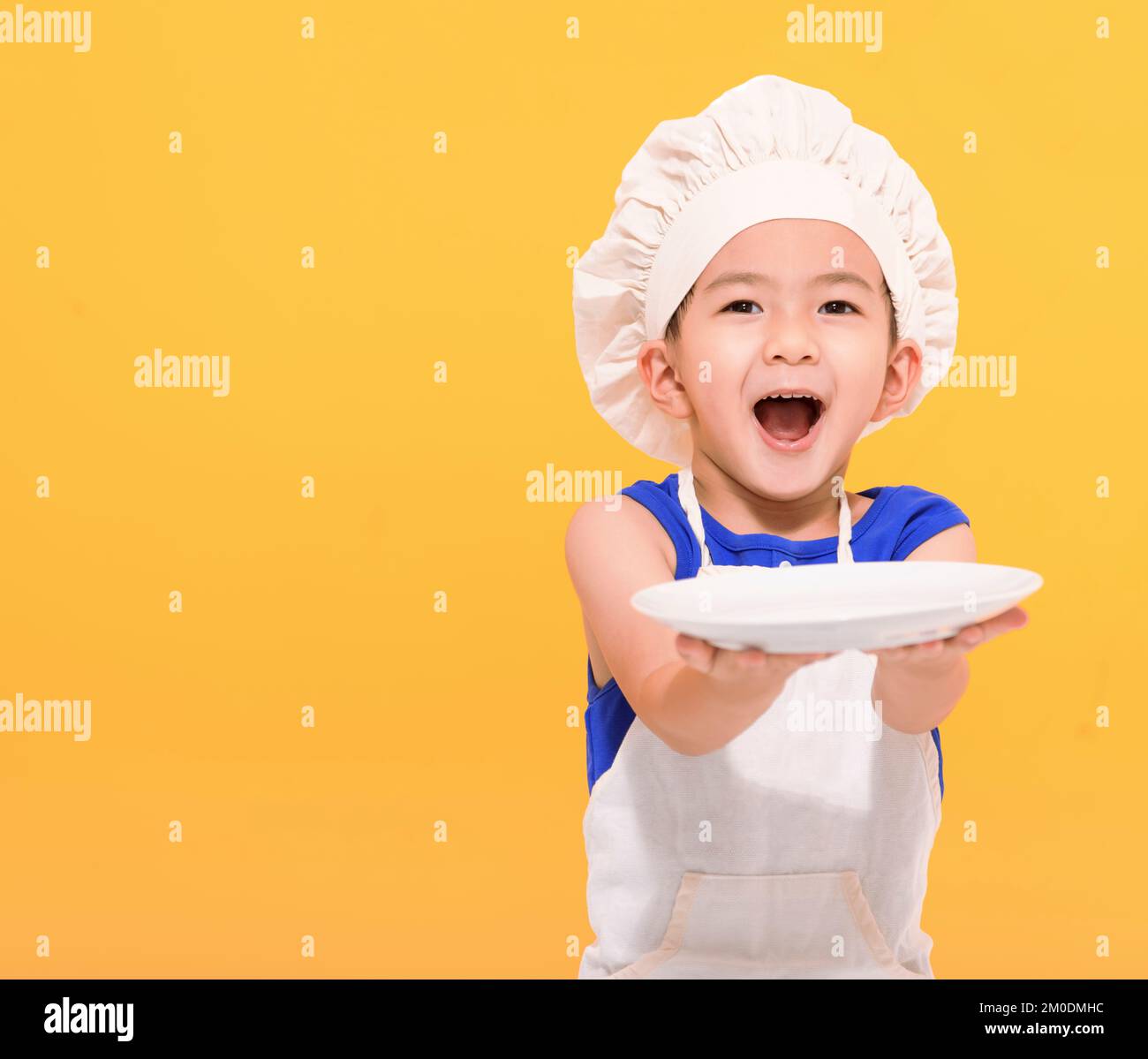 Happy little boy in chef uniform showing empty dish on yellow ...