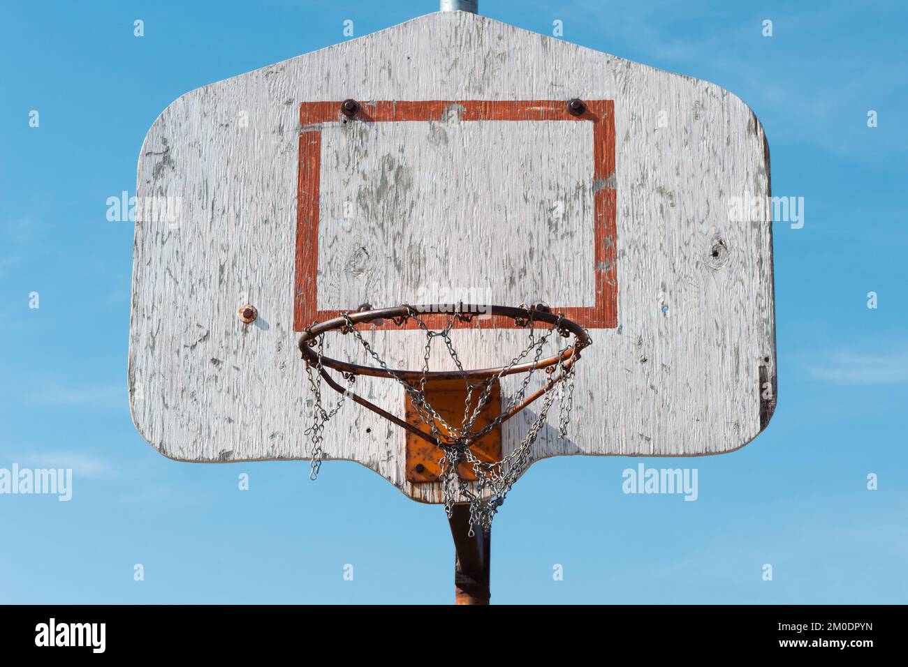 Close up of an aged wooden basketball backboard and red hoop with blue ...