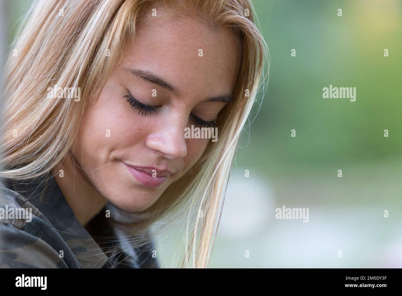Side portrait of young blond coy woman with downcast gaze sitting in a ...