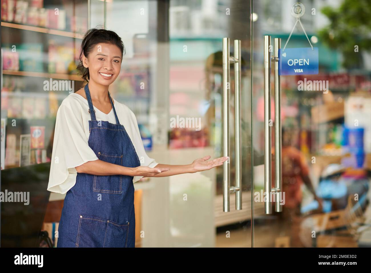 Positive supermarket worker inviting customers in grocery store Stock ...