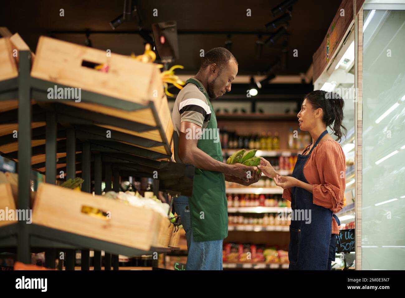 Supermarket workers in aprons discussing where to put fresh fruits ...
