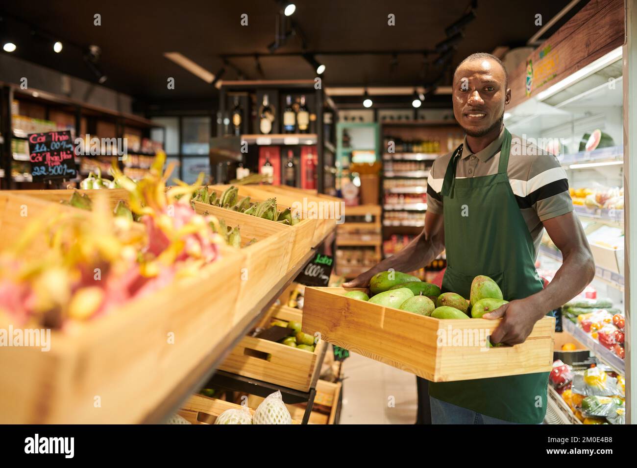 Supermarket worker bringing box of mangoes to produce department in ...