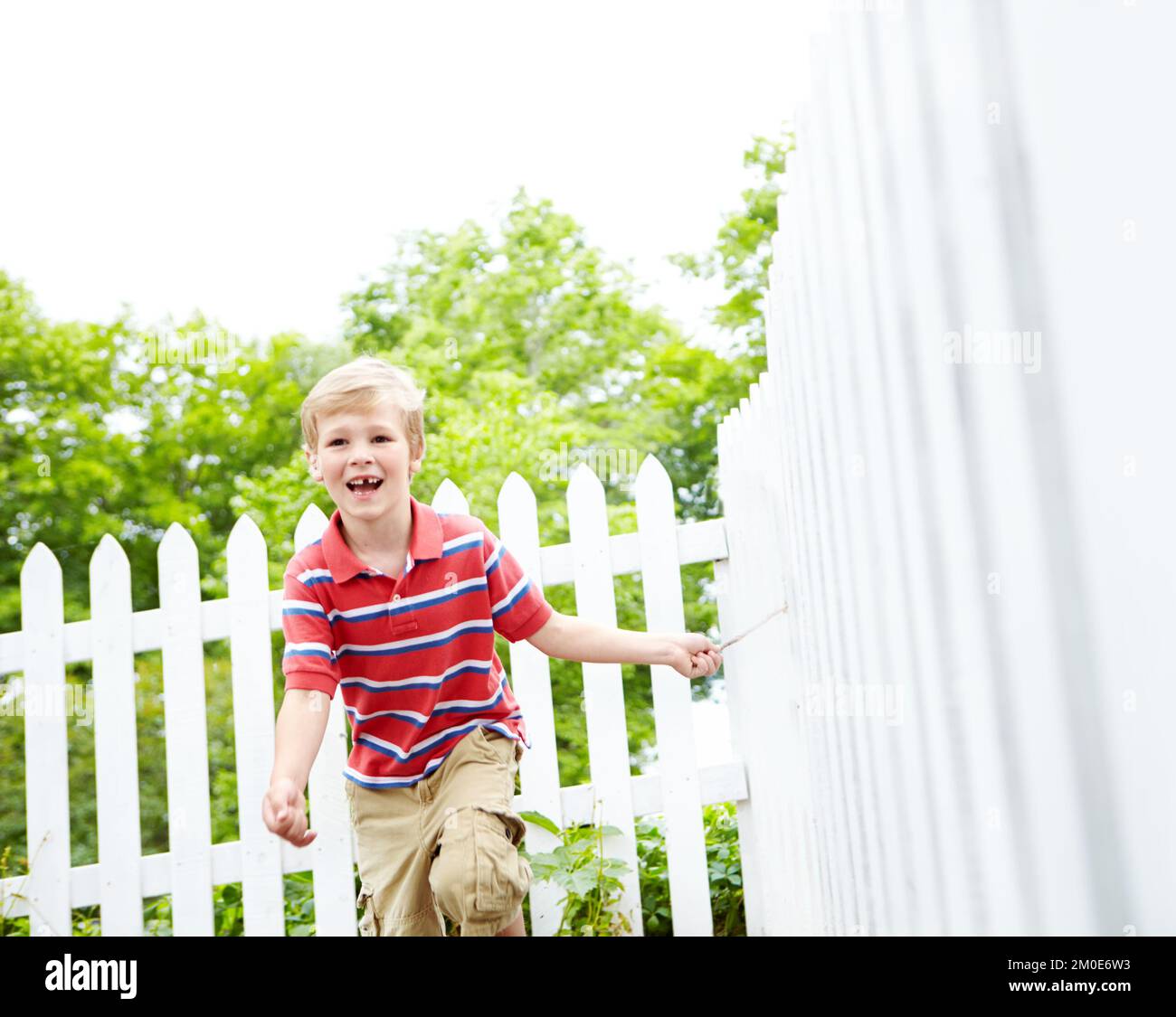 Oh to be young again. A cute young boy running a stick along a white ...
