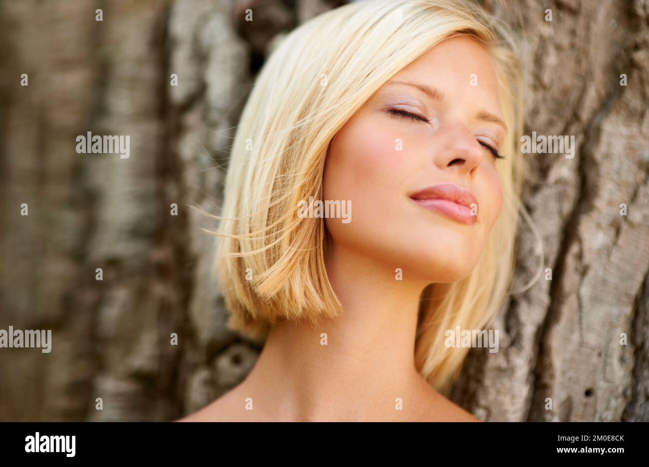 Natural beauty up close. Relaxed young woman leaning against a tree ...