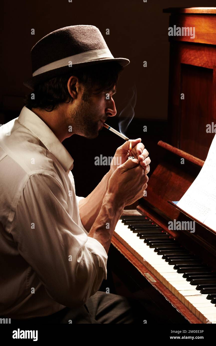 Moody musician. Profile of a handsome man having a smoke at his piano ...