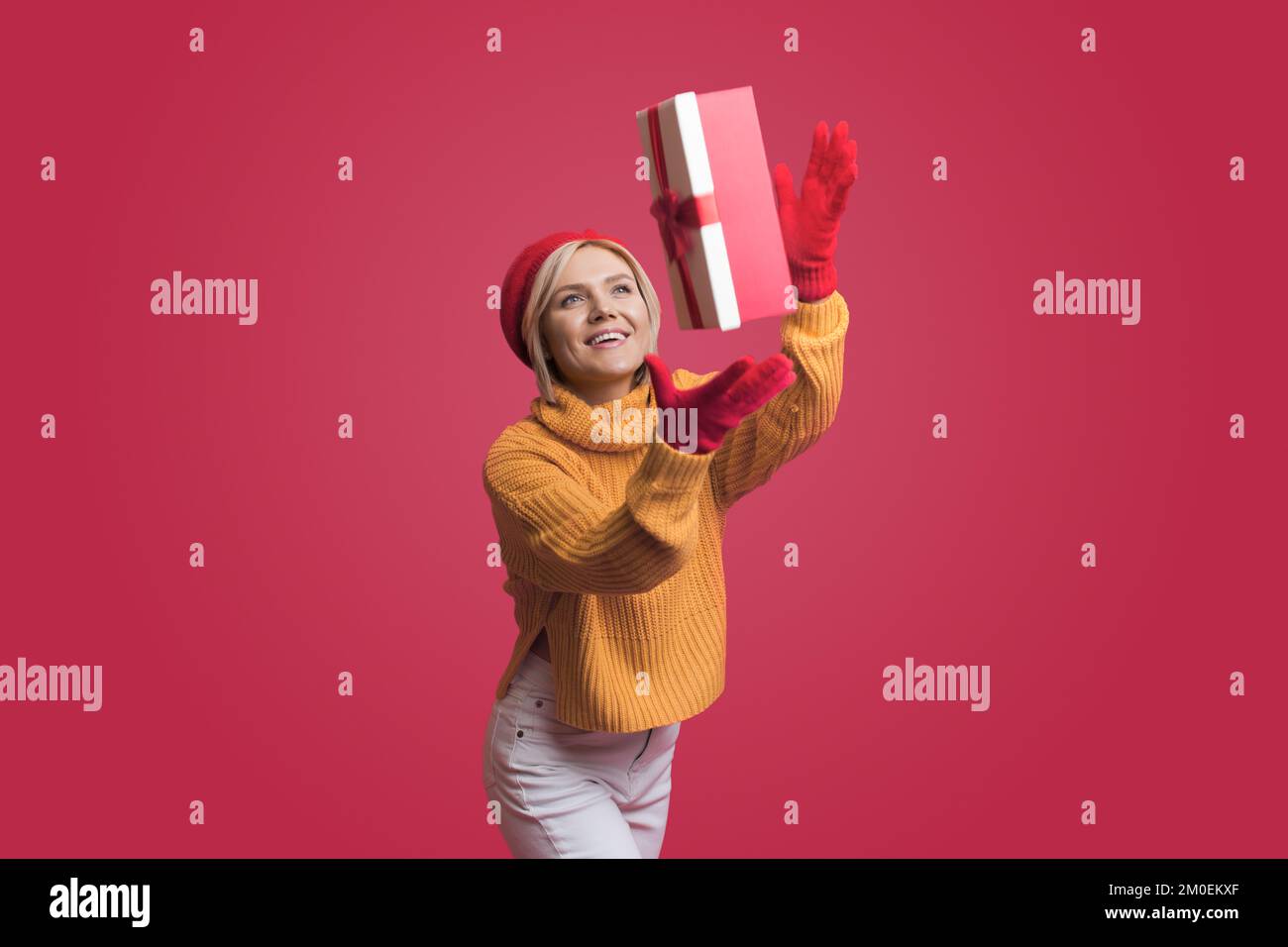 Woman blowing up a gift box while standing isolated on pink background ...