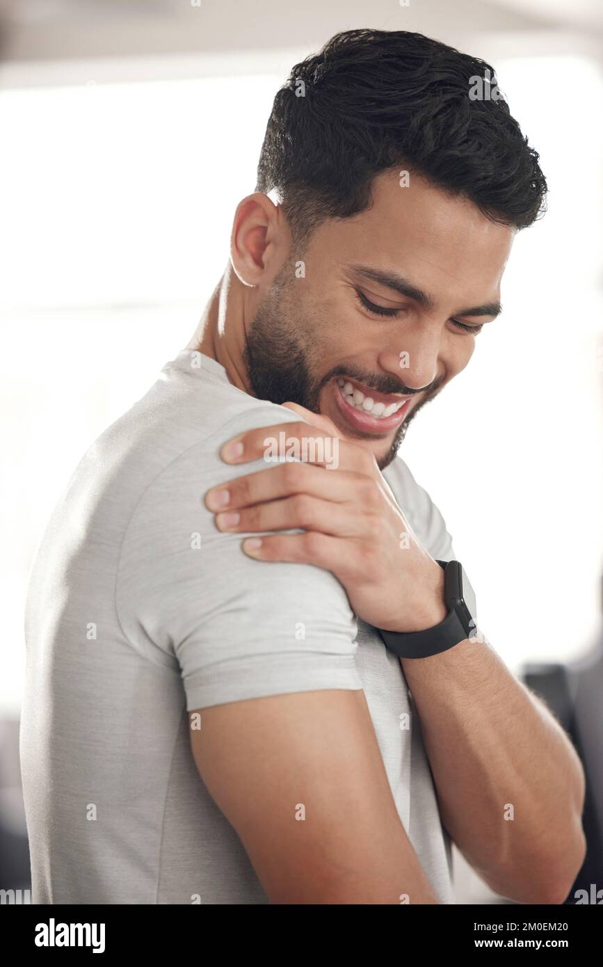 One young hispanic man holding his sore shoulder while exercising in a ...