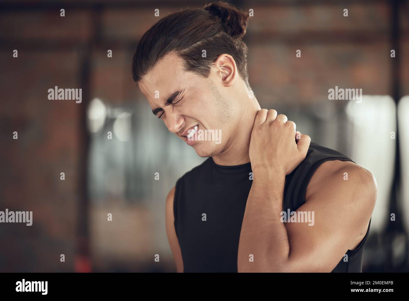 Bodybuilder experiencing a neck cramp in the gym. Fit young man with neck pain in the gym ...
