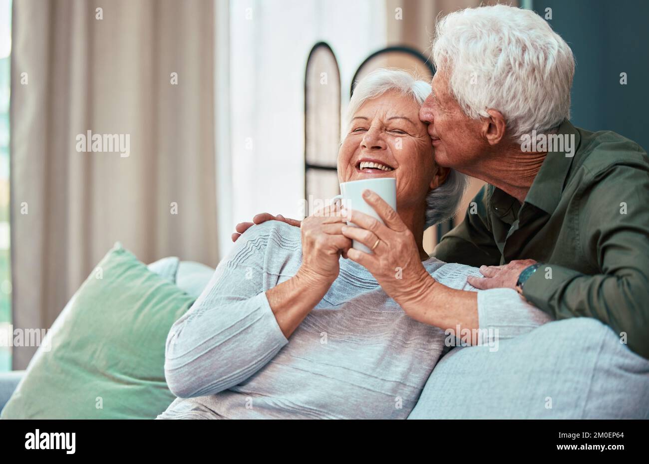 Kiss, coffee and senior couple laughing, talking and smile during retirement in the living room ...