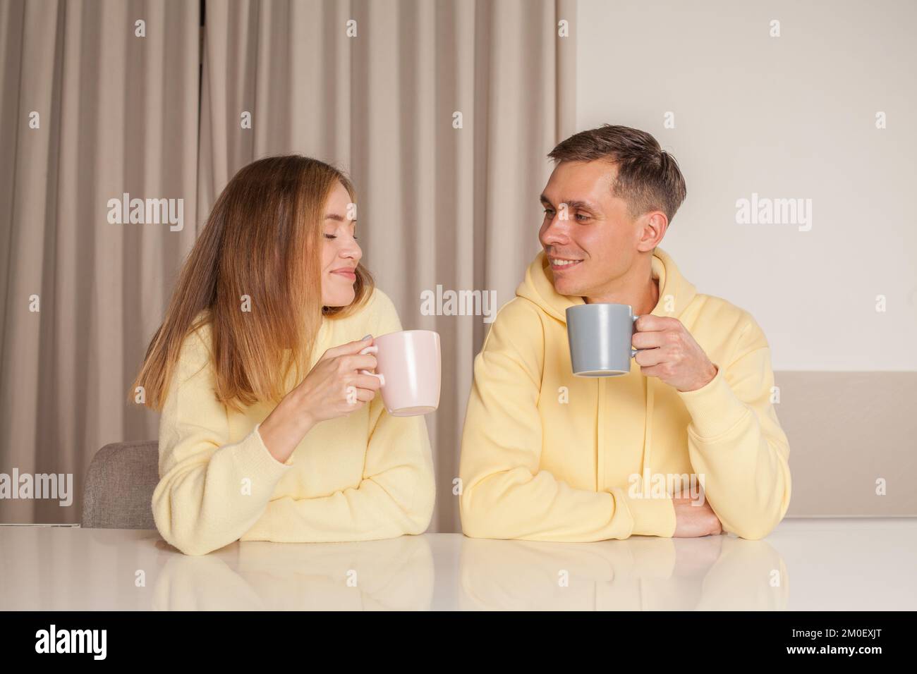 Lovely couple drinking something from the cups and sitting by the table ...