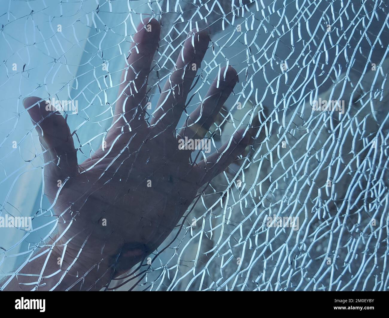 Hand behind blue broken glass with white cracks Stock Photo - Alamy