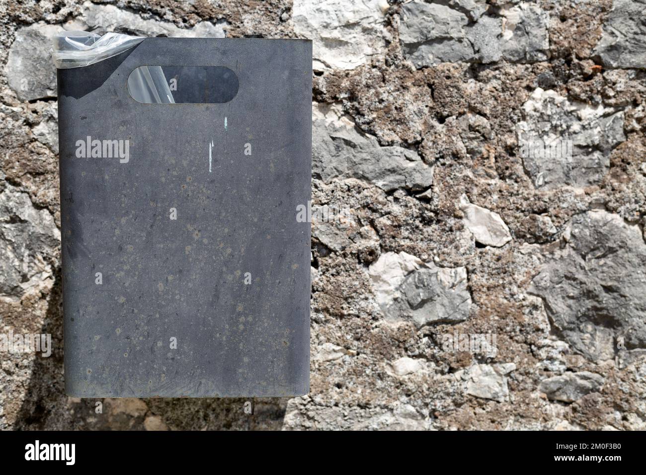 Horizontal photo of grey metal trash can on left side with stone wall ...