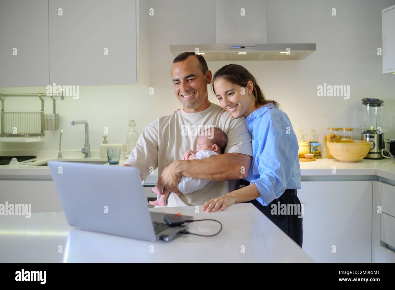 Happy parents with newborn child using laptop in kitchen Stock Photo ...