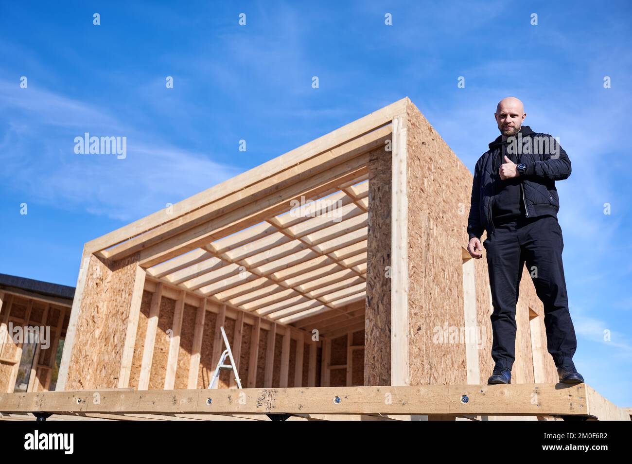 Developer building wooden frame house in Scandinavian style barnhouse. Bald man standing on ...