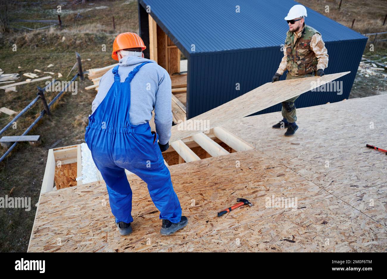 Carpenters mounting wooden OSB panel on rooftop of future cottage. Men ...