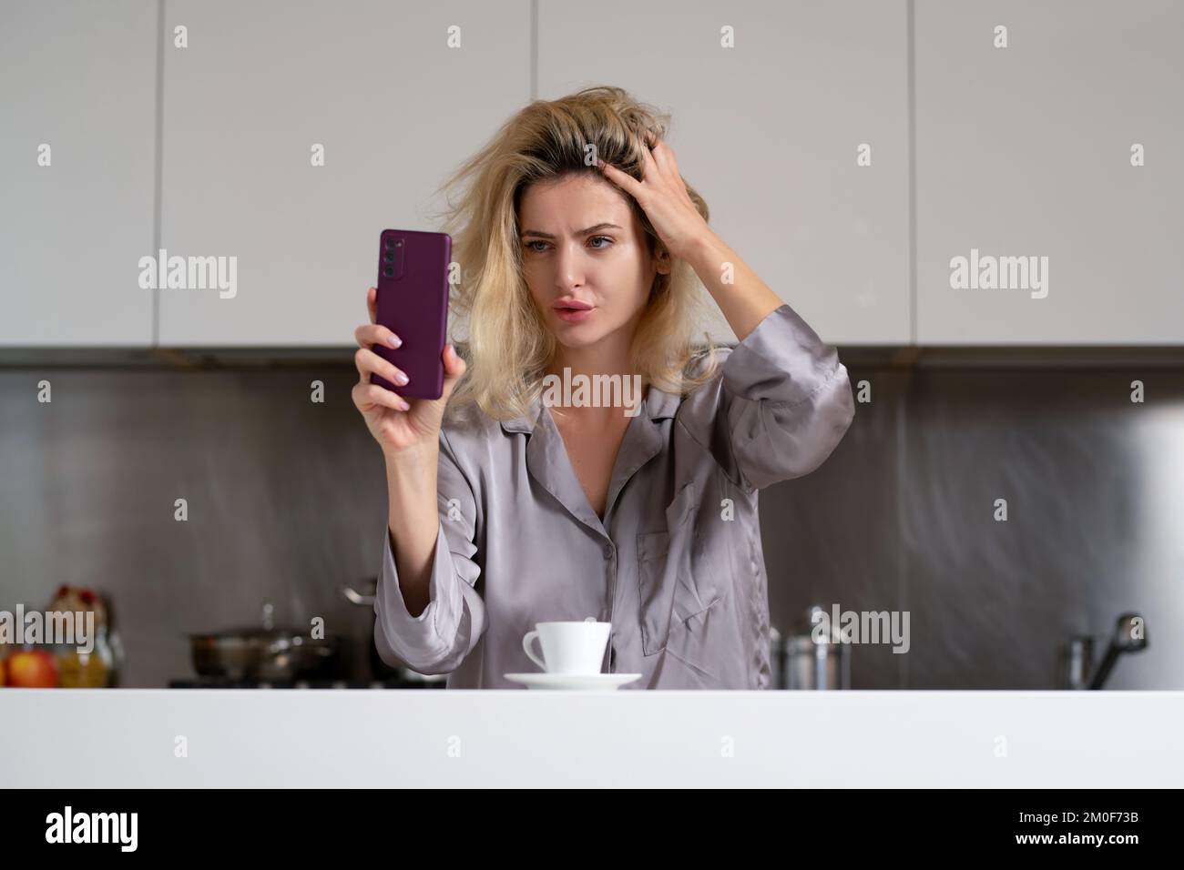 Sad woman chatting on mobile phone on kitchen at home. Housewife mood ...