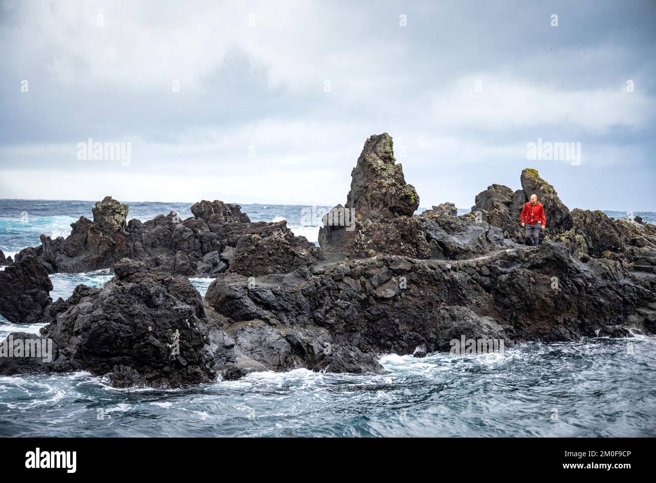 Man walking on rough volcanic rock at the coast of São Jorge, Azores ...