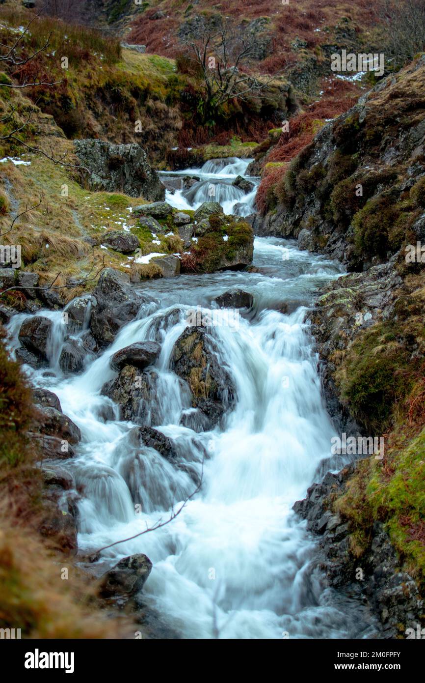 A vertical shot of a waterfall flowing in a valley in a cold weather ...