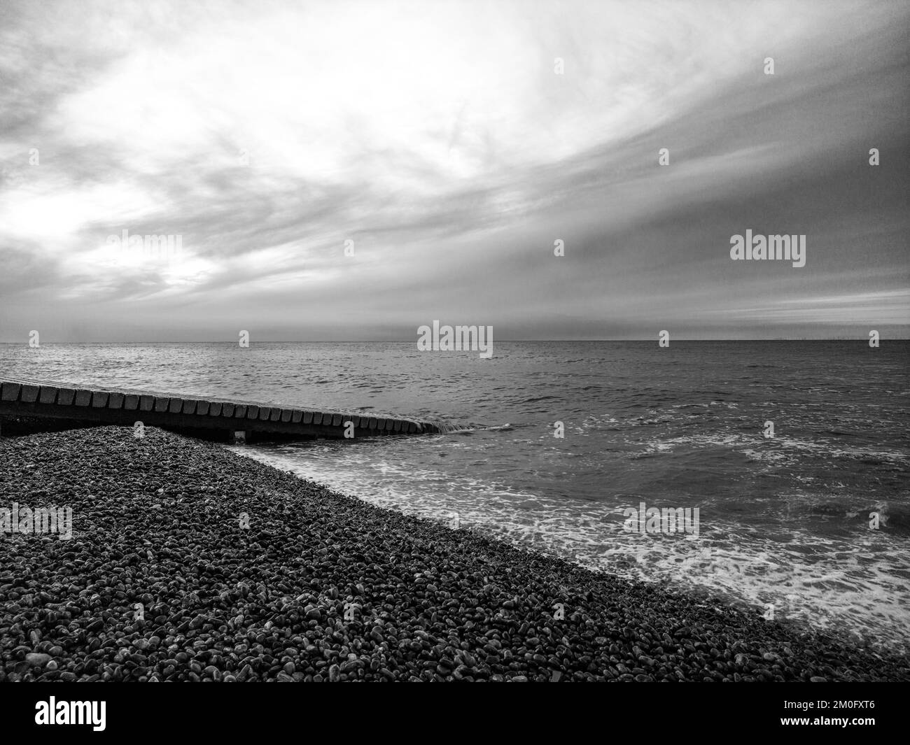 A grayscale of a rocky beach with shallow sea waves hitting the ...
