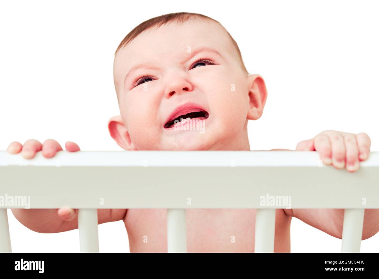 A sad baby is crying in a crib, holding onto the handrails, isolated on ...