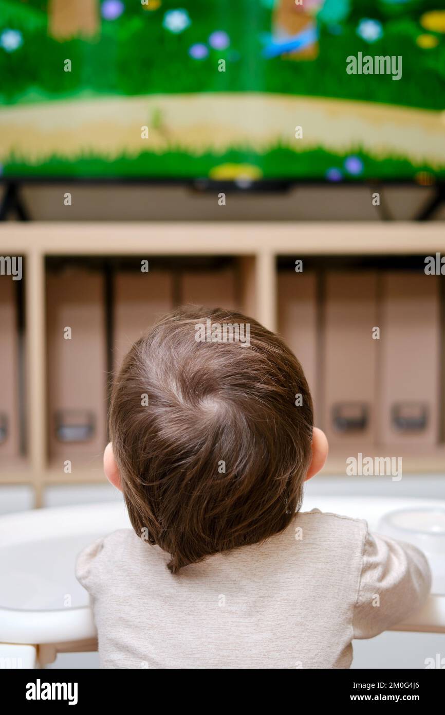 Happy toddler baby boy is watching cartoons on a big TV screen. A child ...